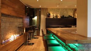 Uma área de bar moderna com piso de madeira, banquetas verdes e uma parede de destaque em pedra.