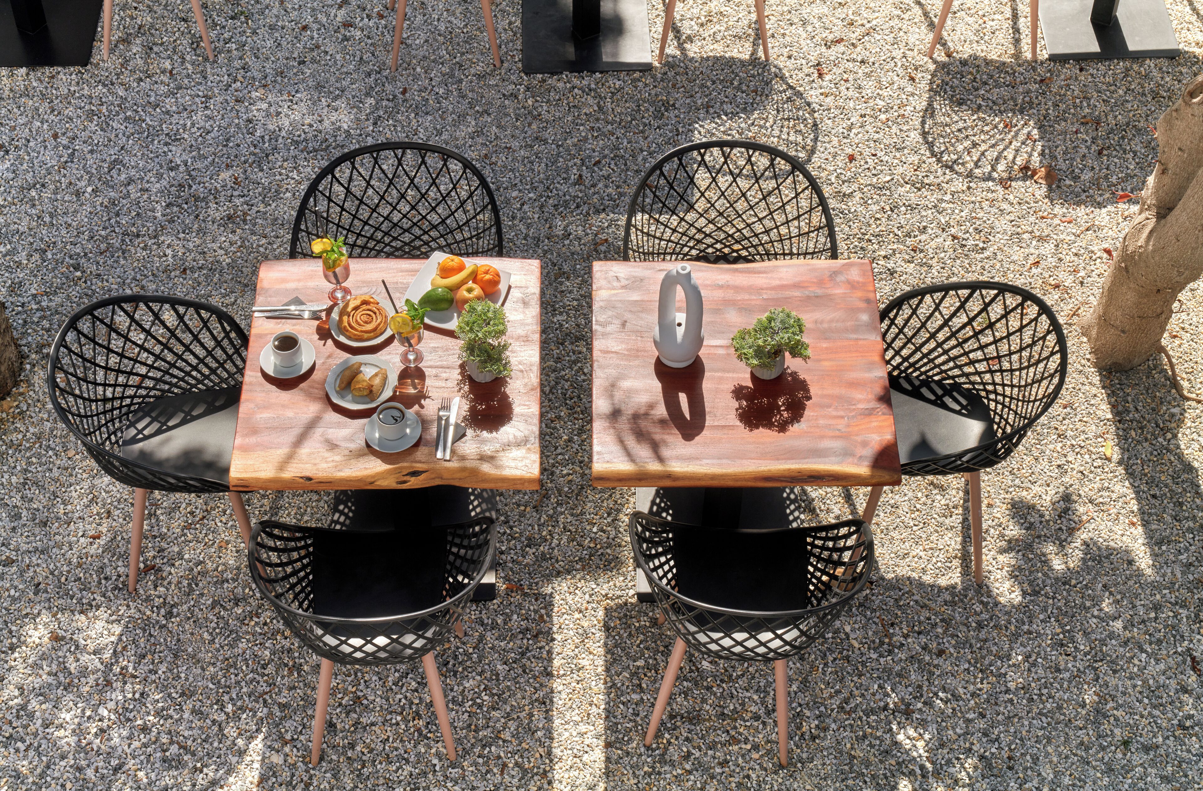 Duas mesas de madeira com cadeiras de metal, cada uma com pratos, talheres e pequenos vasos de plantas.