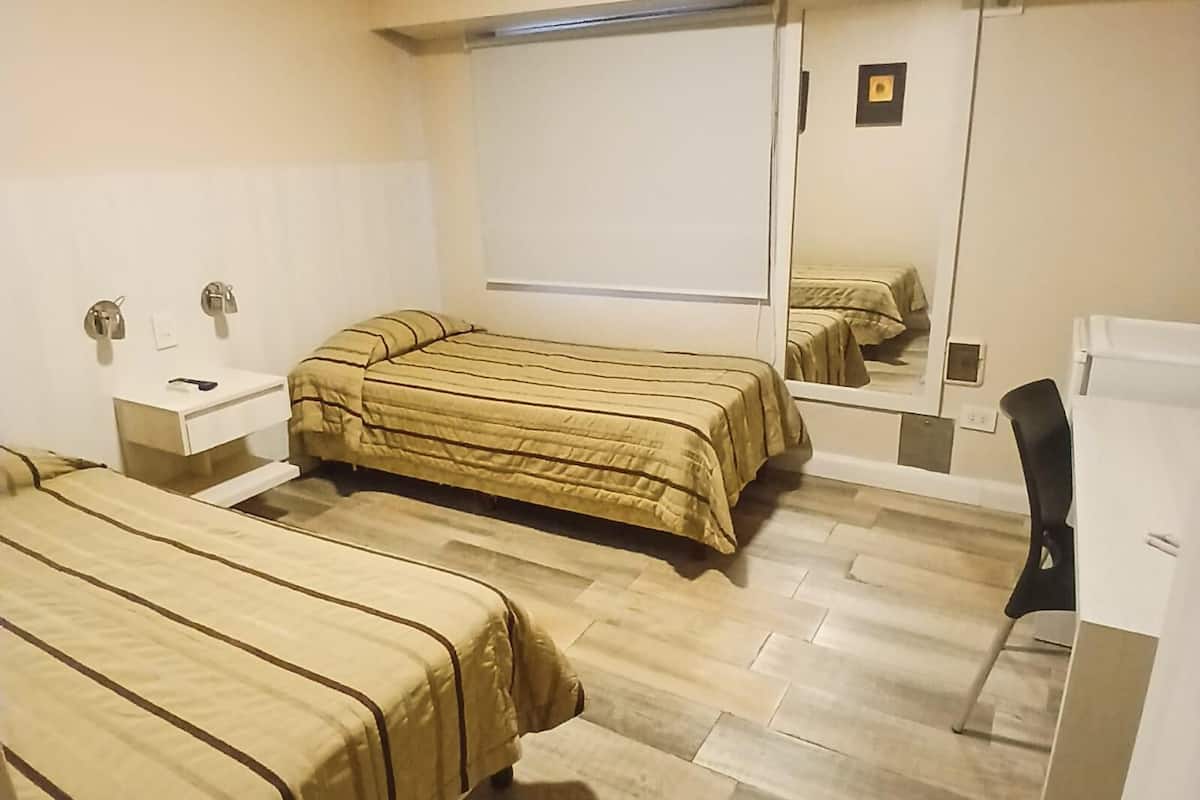 Quarto de hotel com duas camas, uma escrivaninha, uma cadeira, um espelho e um ar condicionado.