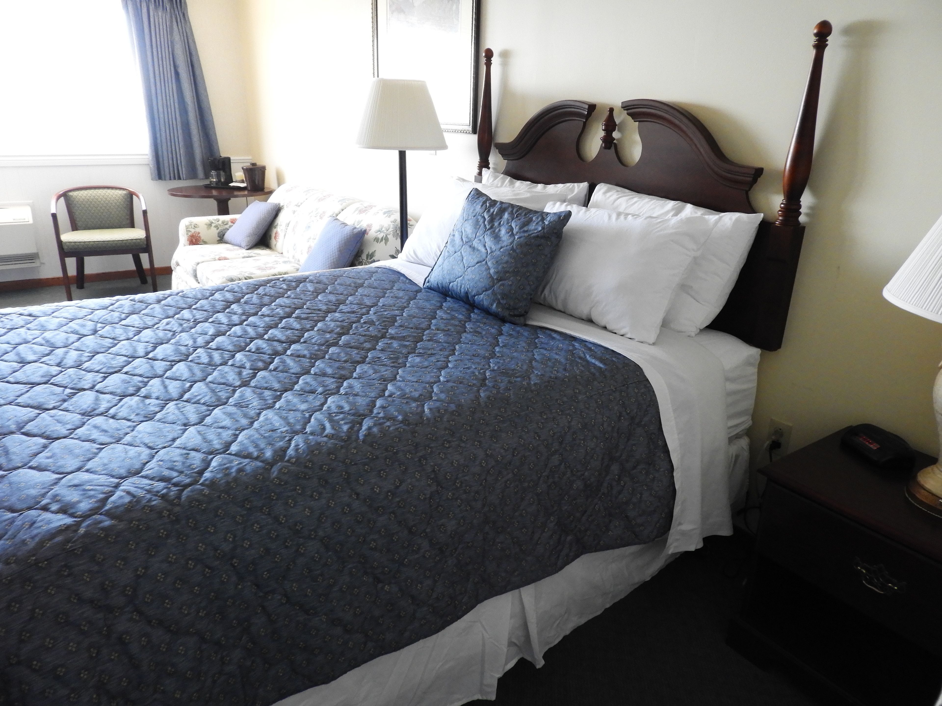 Uma cama bem arrumada com um edredom azul, cabeceira de madeira e roupa de cama branca.