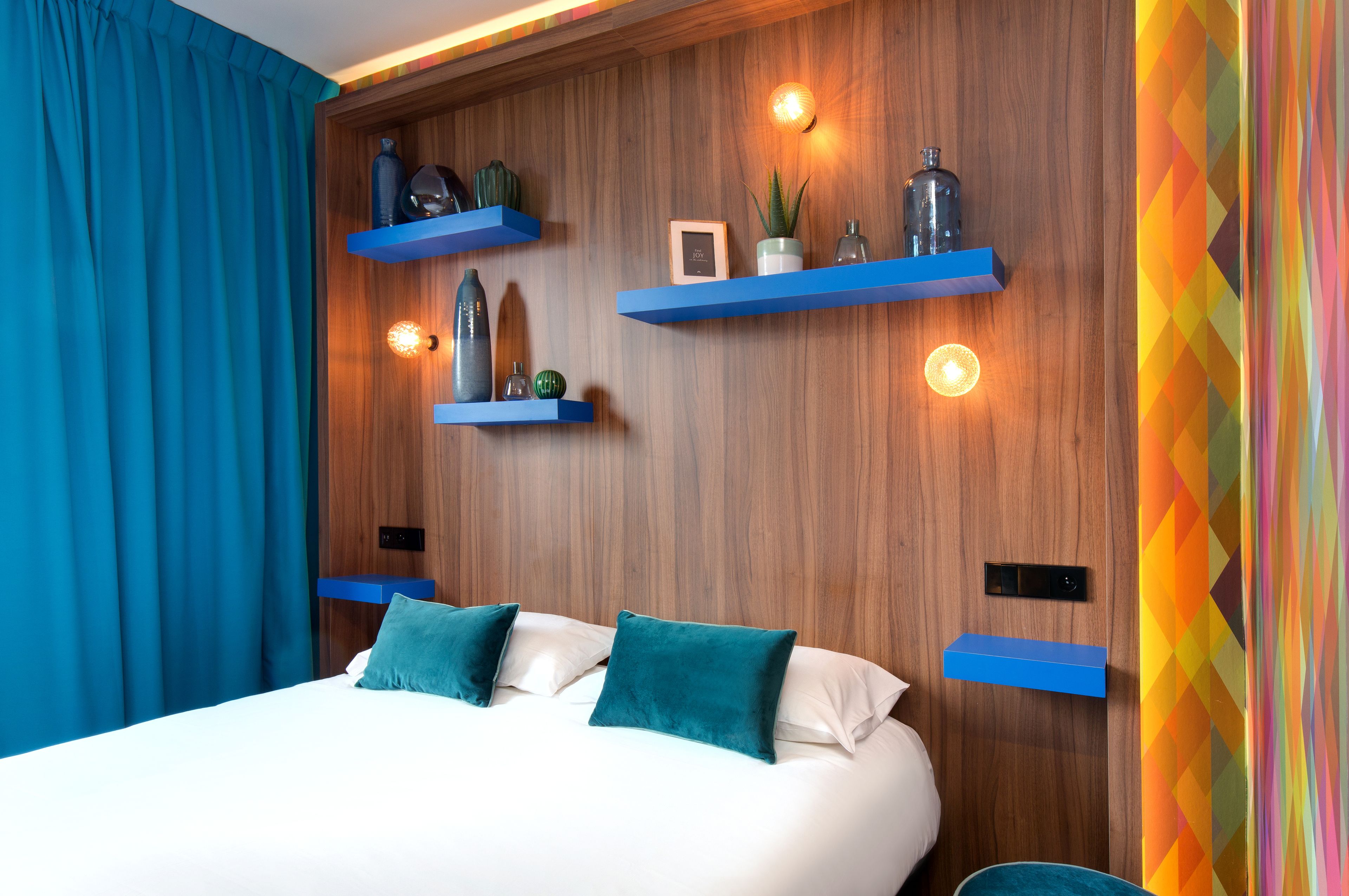 Quarto moderno com cabeceira de madeira, prateleiras azuis suspensas e cama com almofadas verde-água.