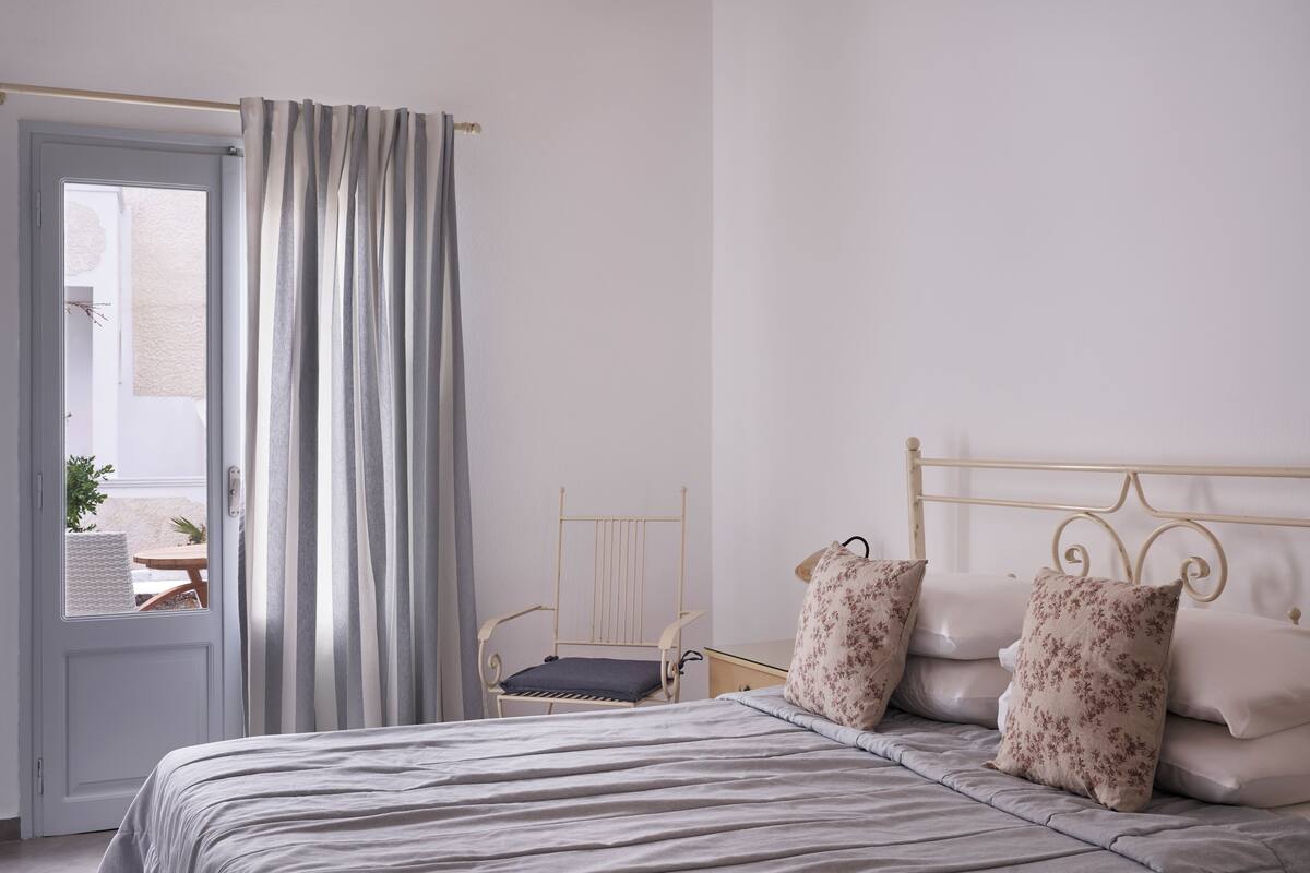 Quarto com cama, cadeira, escrivaninha e janela com cortinas.