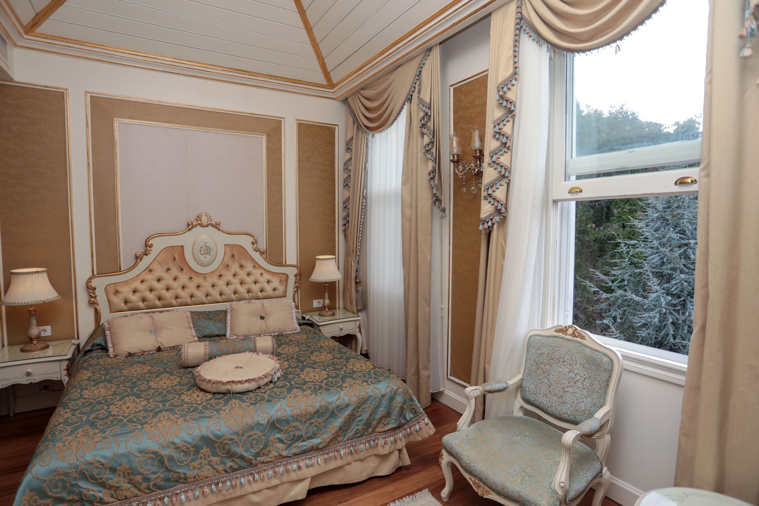 Quarto com cama grande, uma cadeira e janela com vista para árvores.