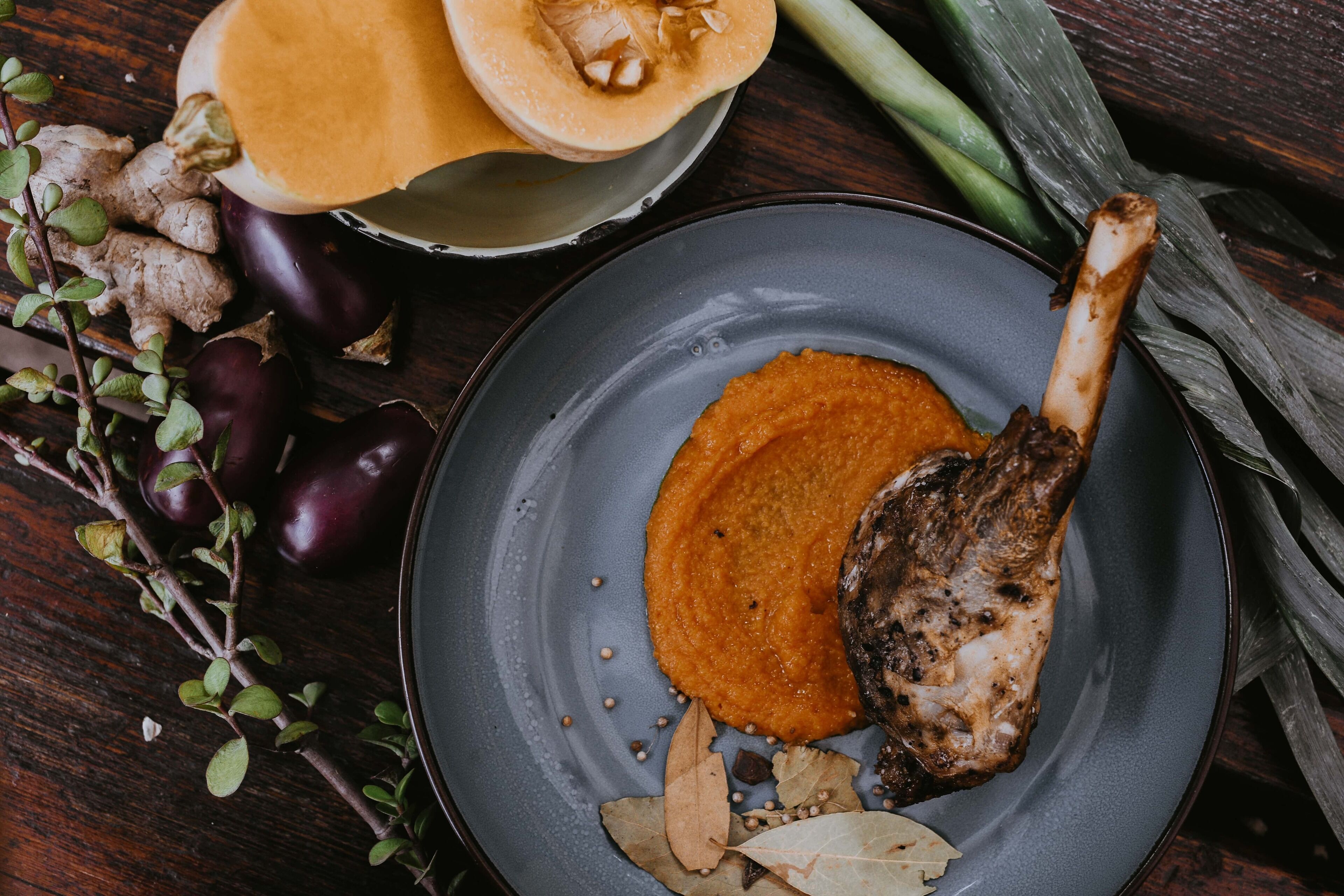 Um prato com carne grelhada, um purê de laranja cremoso e alguns temperos.
