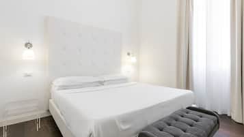 Quarto de hotel moderno com uma cama grande, luminárias de cabeceira, um banco e vista para o exterior.