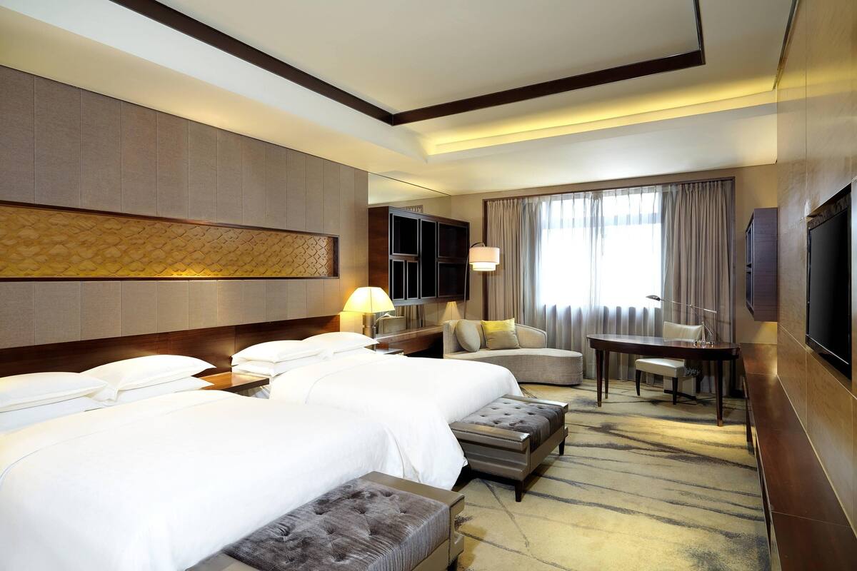 Quarto de hotel com duas camas, um sofá, uma escrivaninha e uma televisão.