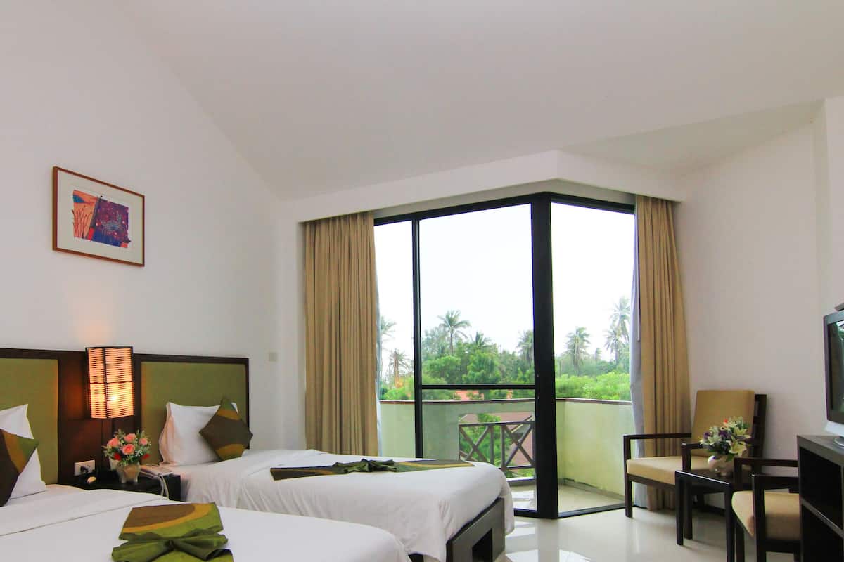 Quarto de hotel com duas camas, uma televisão, varanda com vista para palmeiras e um quadro na parede.