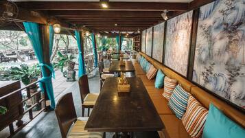 Um restaurante interno com mesas e bancos de madeira, plantas em vasos e obras de arte nas paredes.