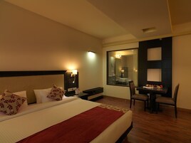 Quarto de hotel com uma cama grande, mesas de cabeceira, uma escrivaninha com cadeira, um espelho e uma pequena mesa com frutas.