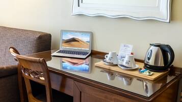 Quarto de hotel com escrivaninha de madeira, um laptop, uma máquina de café e uma xícara de café.