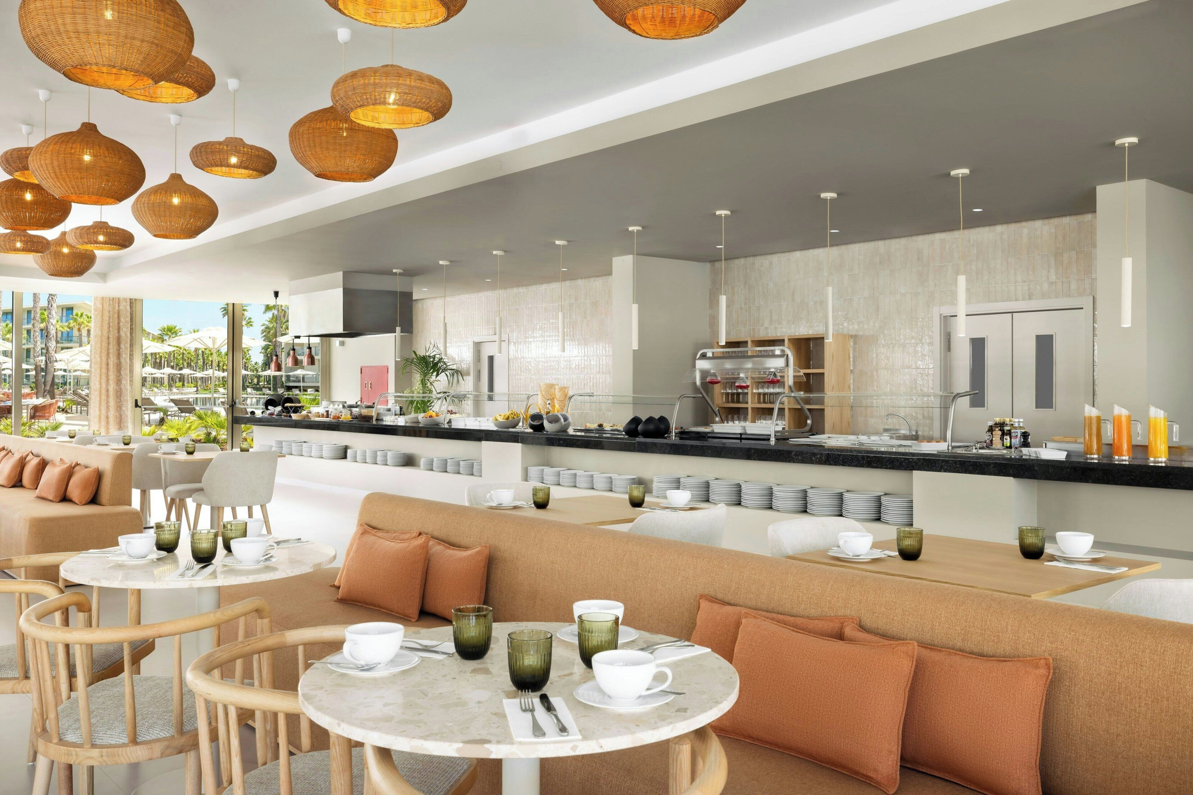 Um restaurante moderno com mesas redondas, assentos acolchoados e luminárias pendentes.