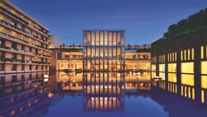 Um hotel com uma piscina refletora na frente, apresentando um edifício moderno em vidro e um edifício tradicional com varandas.