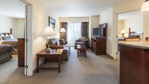 Quarto de hotel com cama, sofá, televisão, escrivaninha e uma mesinha.