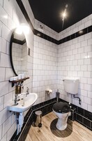 Um banheiro moderno com azulejos brancos, vaso sanitário preto, pia e espelho.
