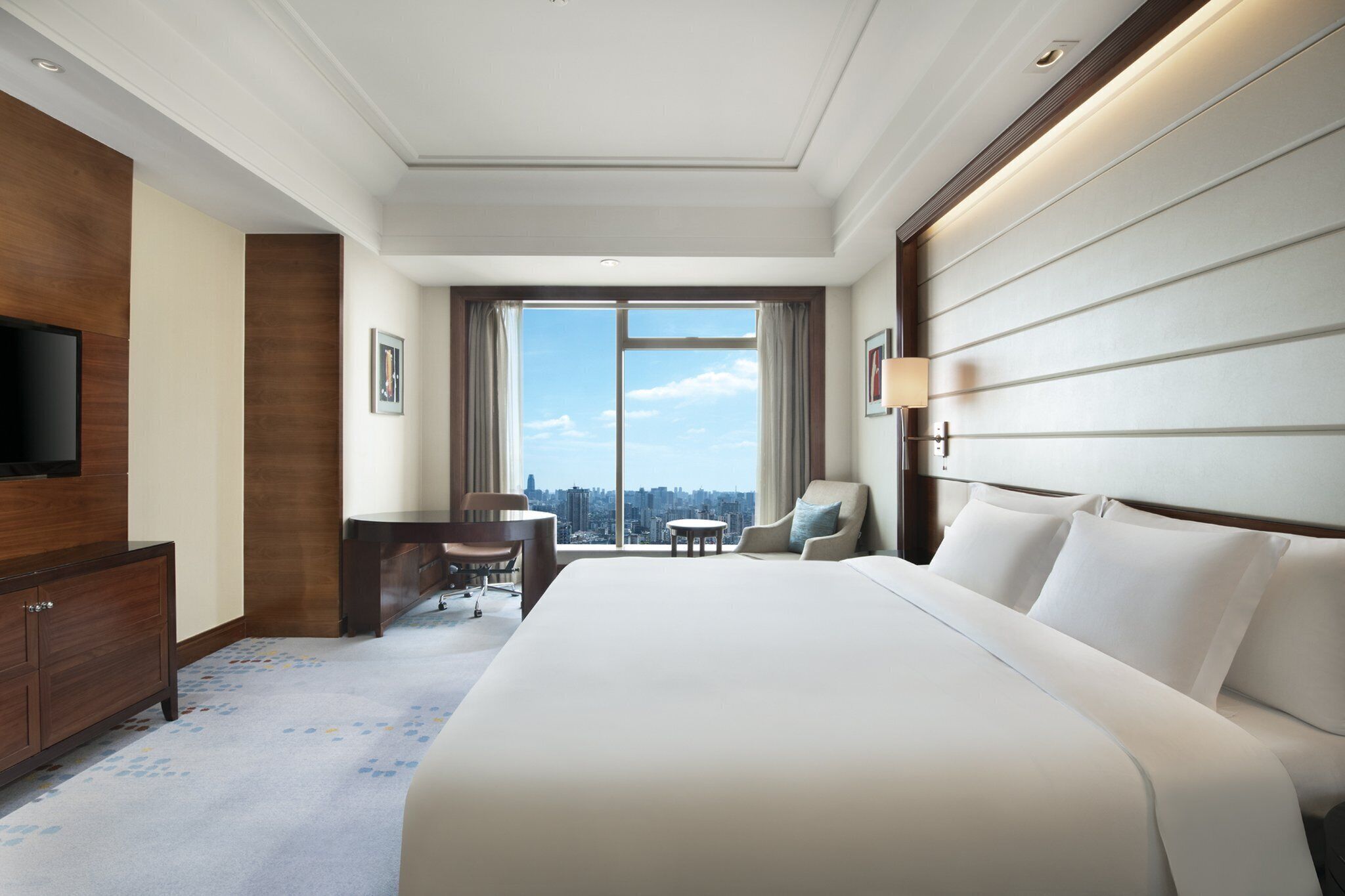 Quarto de hotel com cama grande, escrivaninha, cadeira, televisão e vista para a cidade.