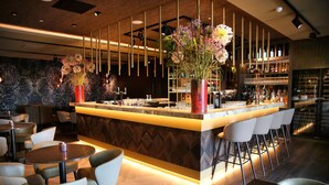 Uma área de bar moderna com ilha central, arranjos de assentos e parede decorada ao fundo.
