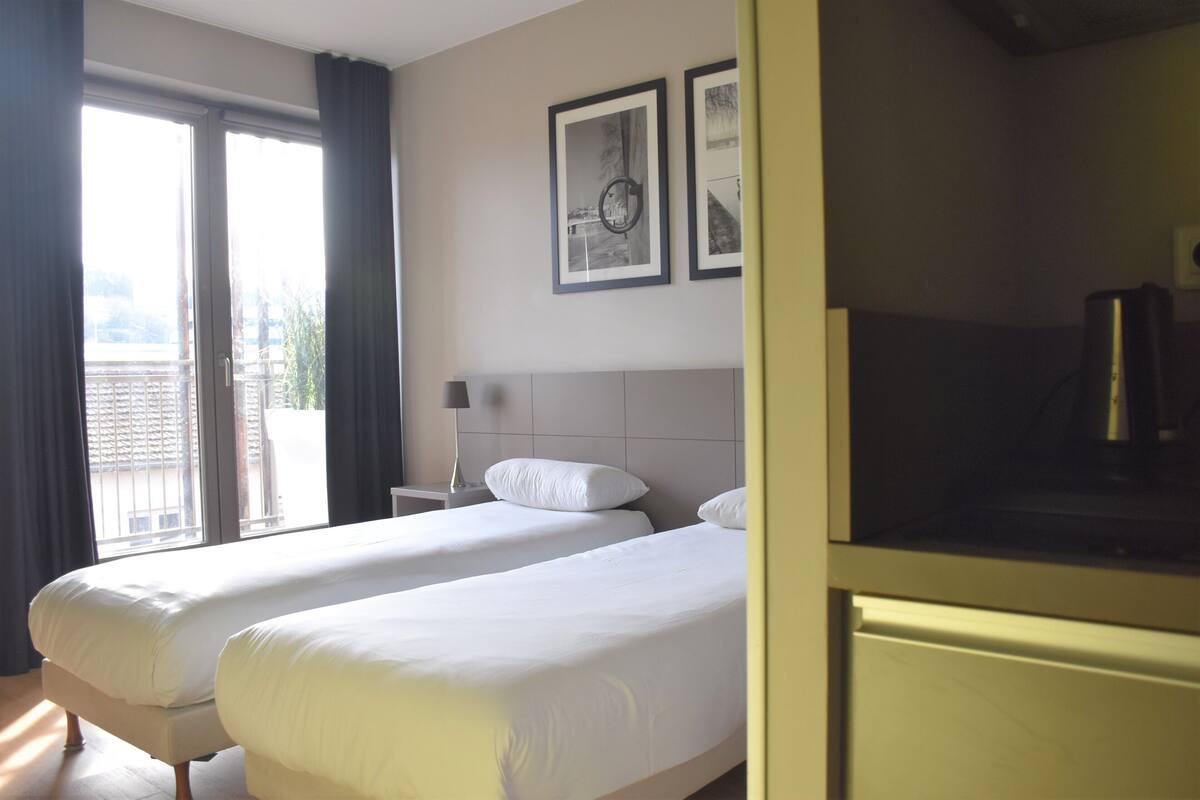Quarto de hotel com duas camas, uma janela grande com cortinas, televisão de tela plana e quadros na parede.