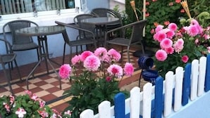 Um pátio com área de estar externa, cerca branca de piquete e flores cor-de-rosa.