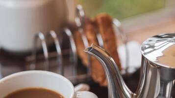 Uma chávena de café sobre um pires, com uma chaleira e cubos de açúcar numa mesa.