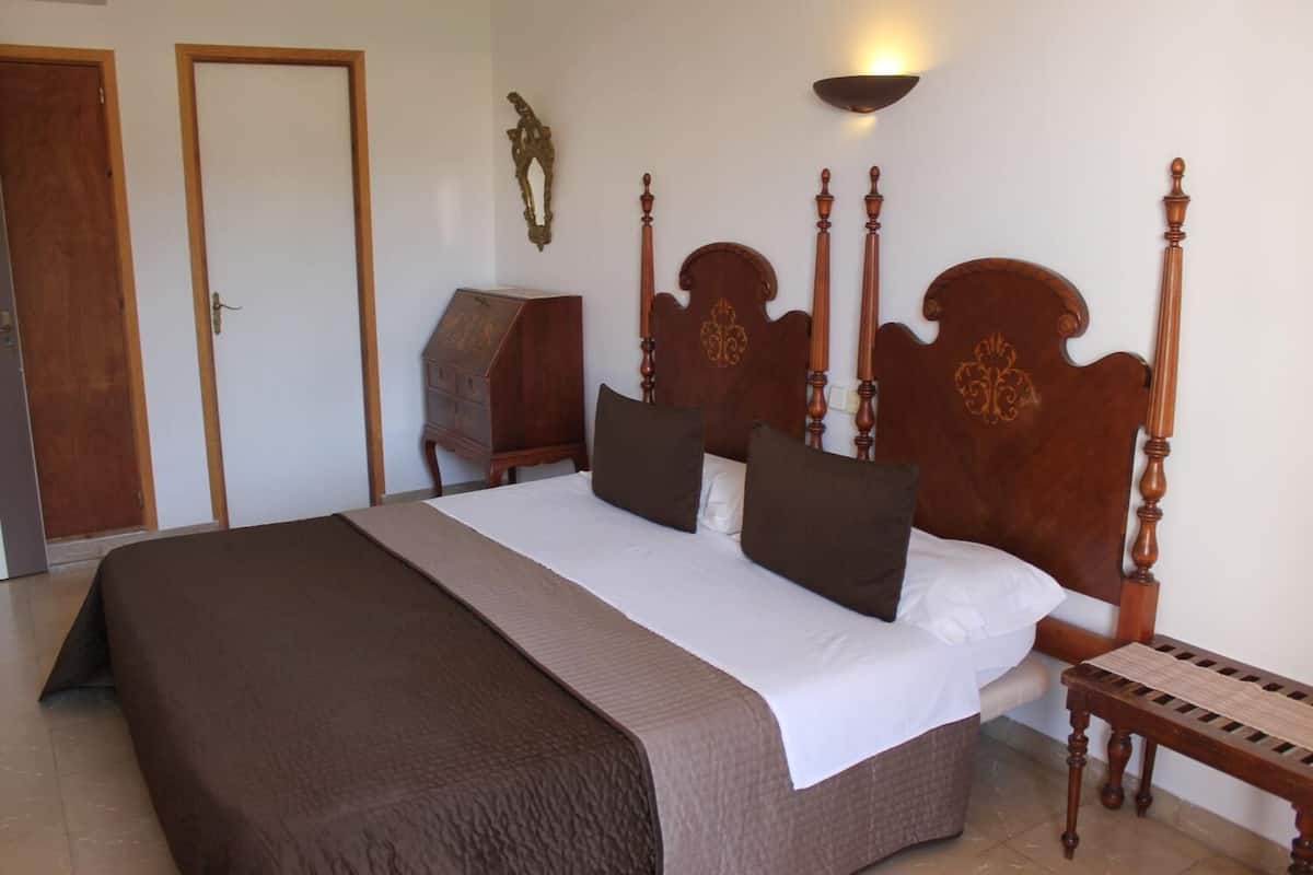 Uma cama bem arrumada com cabeceira de madeira, mesa de cabeceira e luminária fixada na parede.