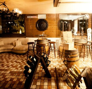 Um espaço de bar acolhedor com barris de madeira, uma mesa redonda e um sofá.