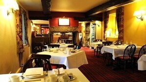 Um restaurante com mesas preparadas para refeições, com carpete vermelho e toalhas de mesa brancas.