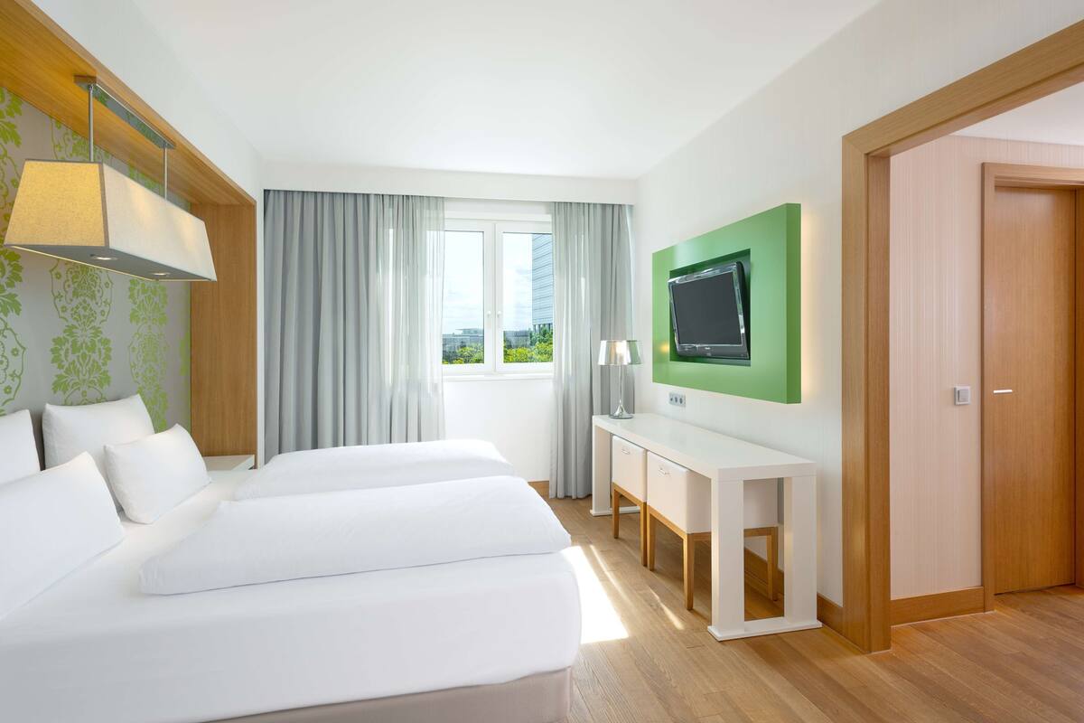 Quarto de hotel com duas camas, televisão, escrivaninha e janela com cortinas.