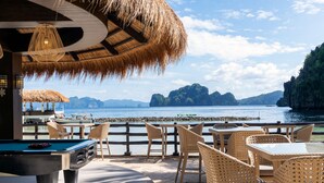 Mesa de bilhar e cadeiras de vime num terraço com vista para o mar e ilhas.