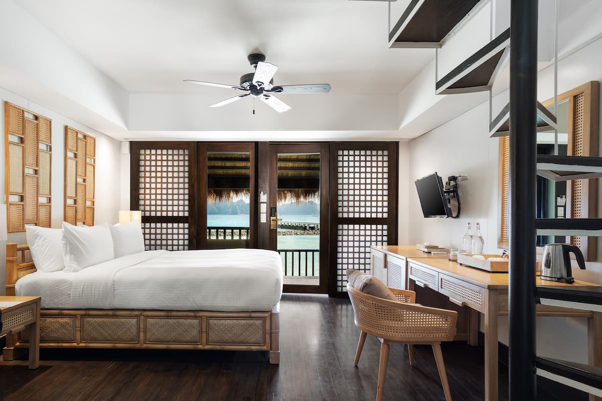 Quarto de hotel com cama, escrivaninha, cadeira e vista pela porta.