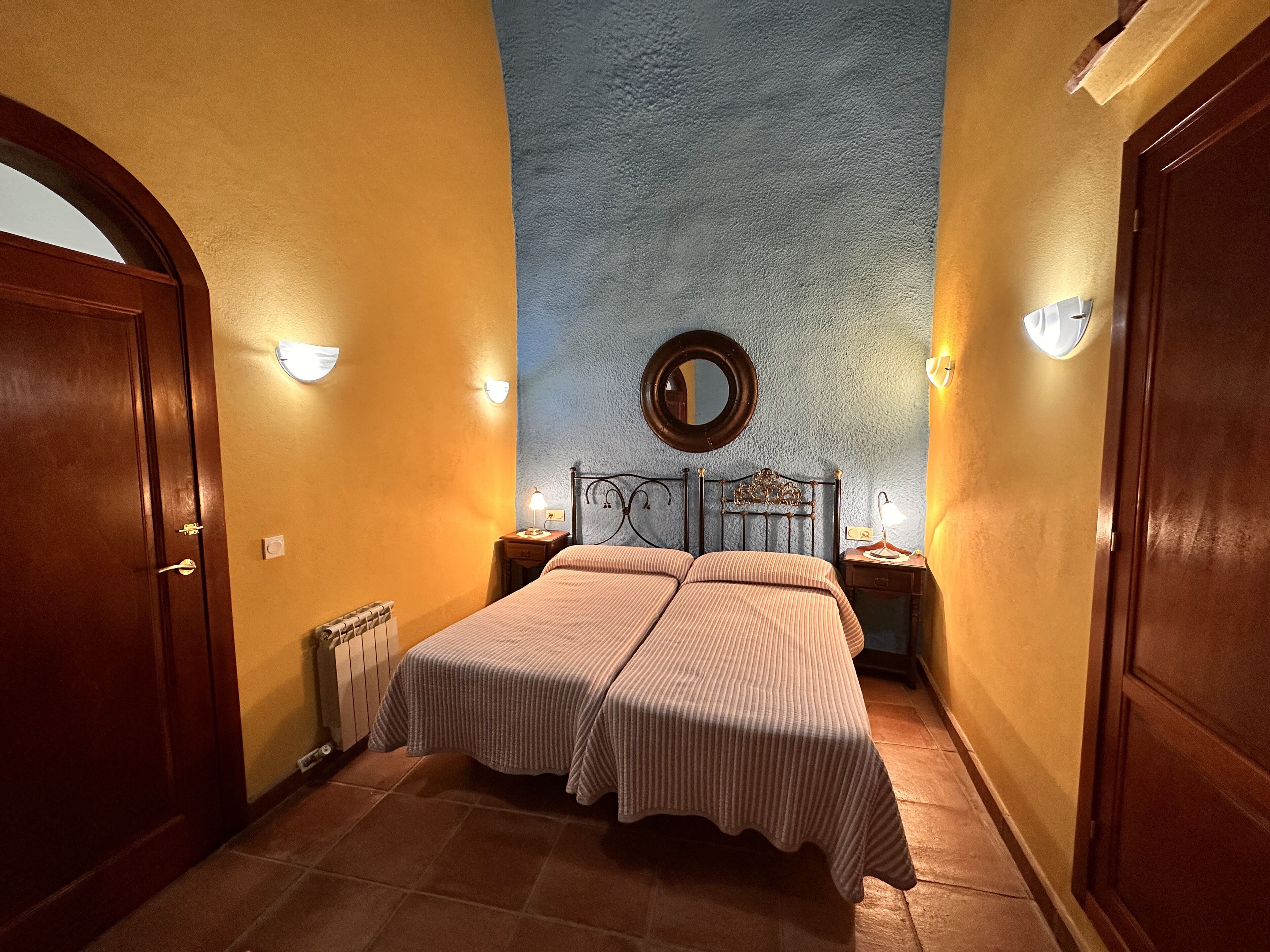 Uma cama de casal com cabeceira, duas mesas de cabeceira, um espelho fixado na parede e um radiador.