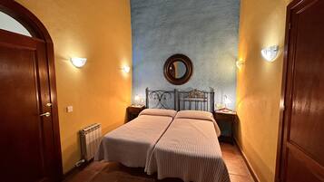 Uma cama de casal com cabeceira, duas mesas de cabeceira, um espelho fixado na parede e um radiador.