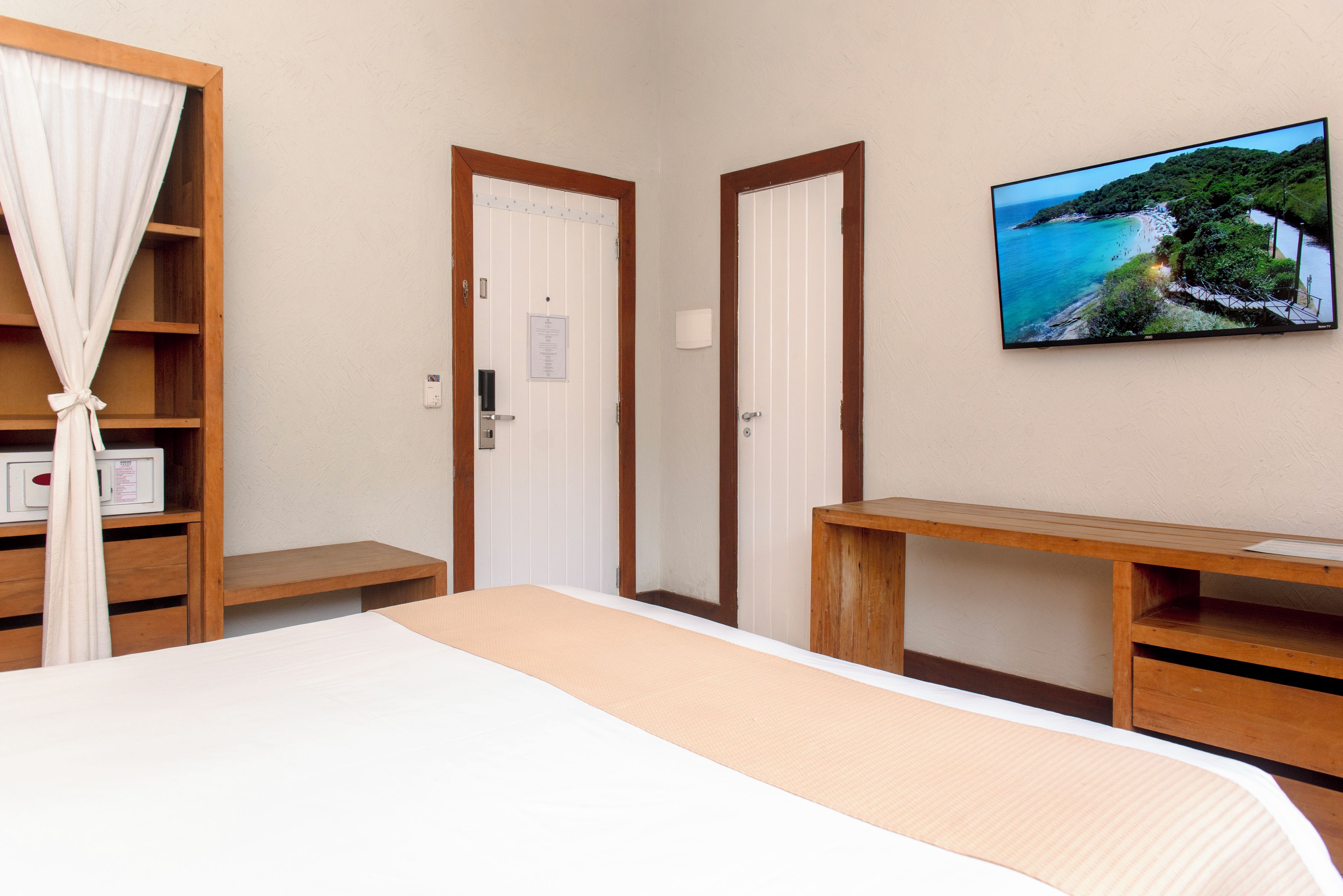 Quarto de hotel com cama, escrivaninha, televisão e guarda-roupa.