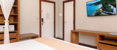 Quarto de hotel com cama, escrivaninha, televisão e guarda-roupa.