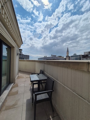 Terraço no telhado com mesa e cadeiras, um abajur e vista para uma mesquita com minarete.