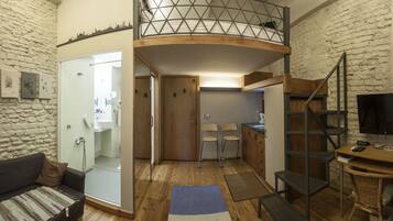 Um espaço compacto com quarto no mezanino, cozinha compacta, área de refeições e banheiro.