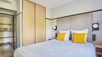 Quarto de hotel moderno com uma cama grande, um guarda-roupa de madeira e uma mesa de cabeceira com abajur.