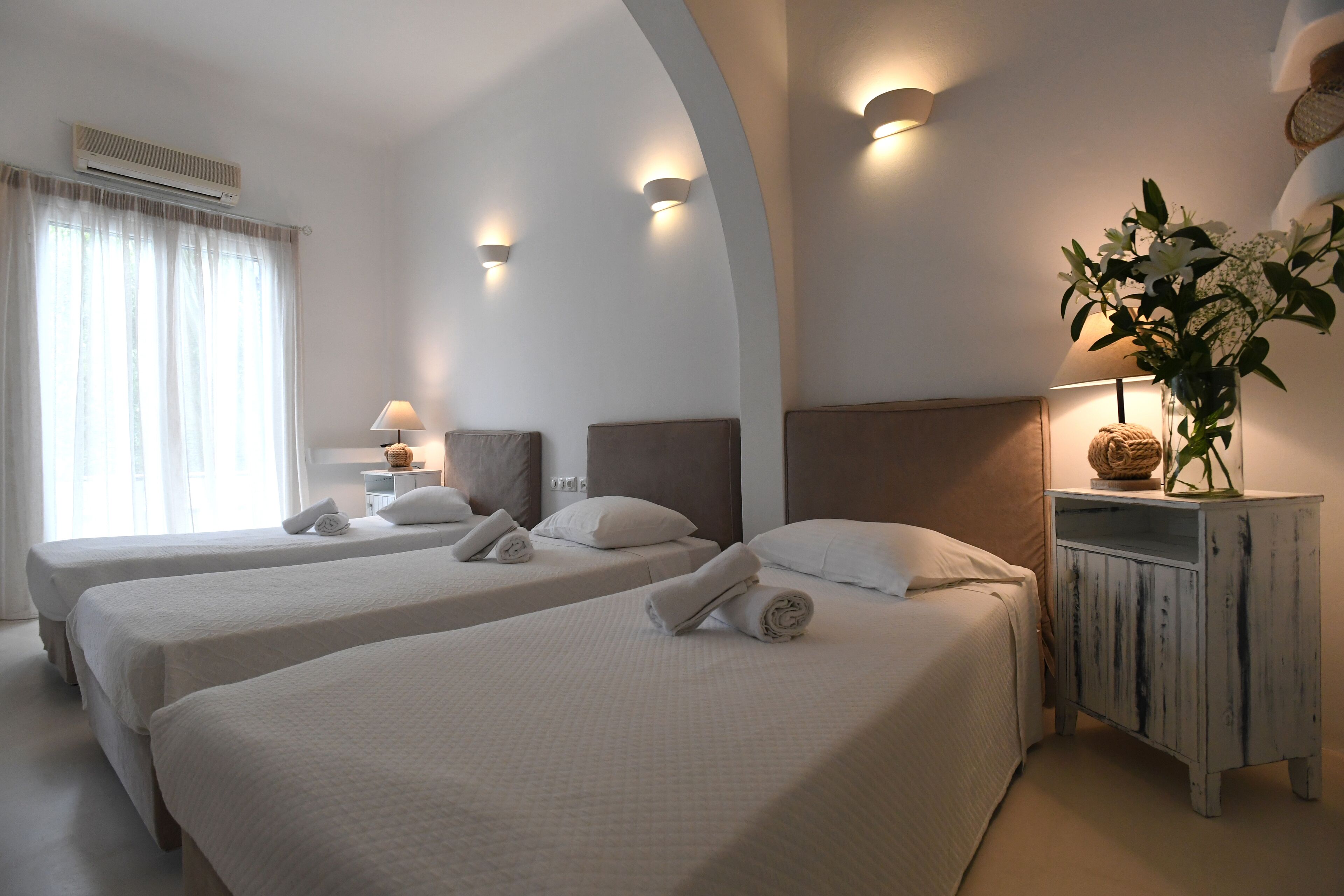 Quarto de hotel com duas camas, uma mesa de cabeceira de madeira, uma luminária e um vaso com flores.