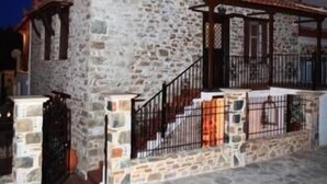 Um edifício de pedra com telhado em telhas, uma escadaria que leva a um alpendre e um chão pavimentado em pedra.