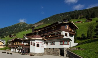 Um hotel alpino tradicional com uma placa grande, várias varandas e uma base de pedra.