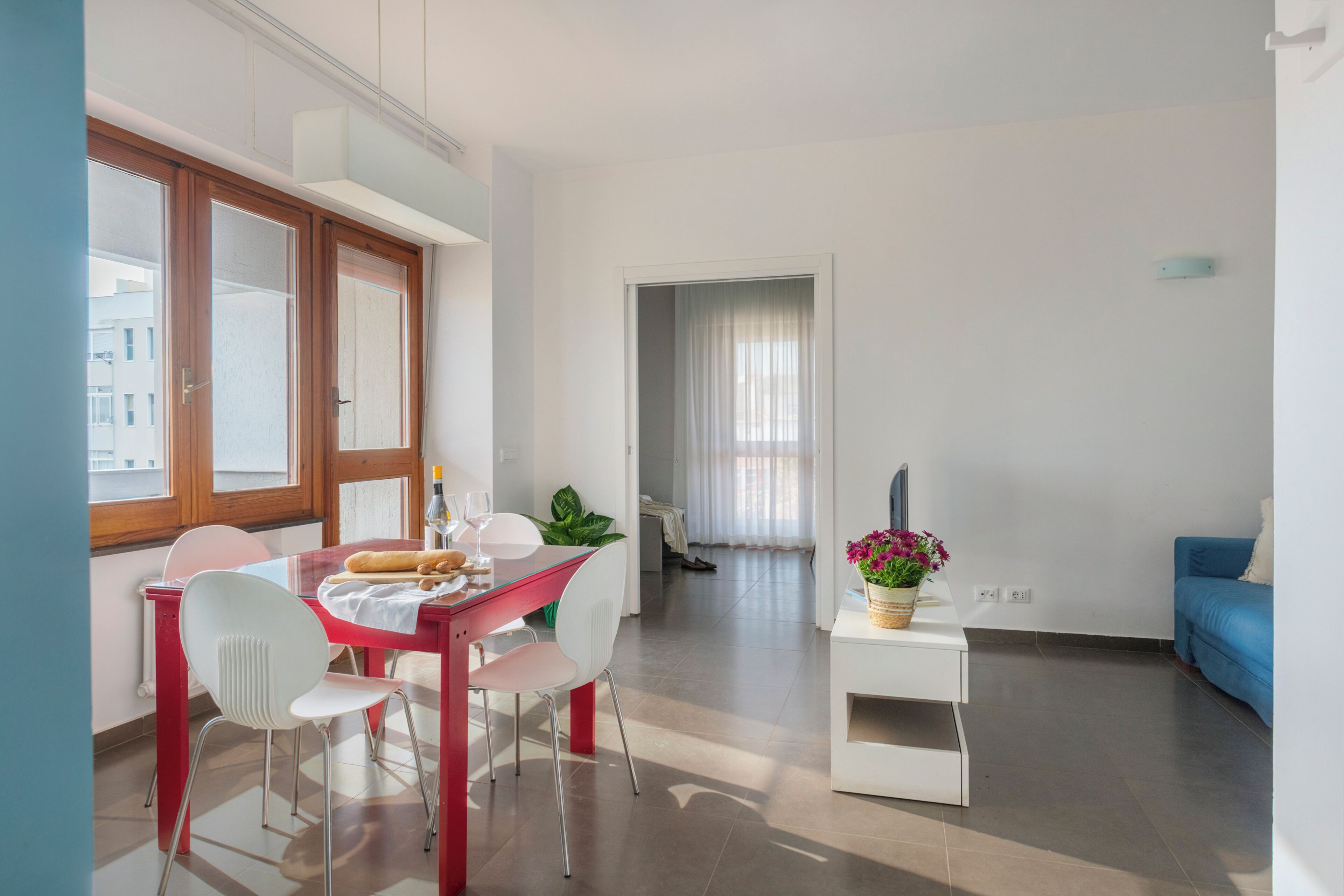 Uma sala de estar moderna com área de jantar, um sofá, uma mesa pequena com uma planta e vista pela janela.