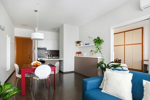 Um espaço de estar moderno com área de jantar, cozinha e um sofá azul com almofada branca.