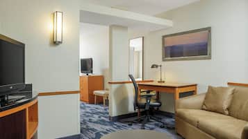 Quarto de hotel com televisão, escrivaninha, cadeira e sofá.