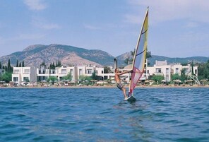 Uma pessoa praticando windsurf em um corpo d'água, com edifícios ao fundo.