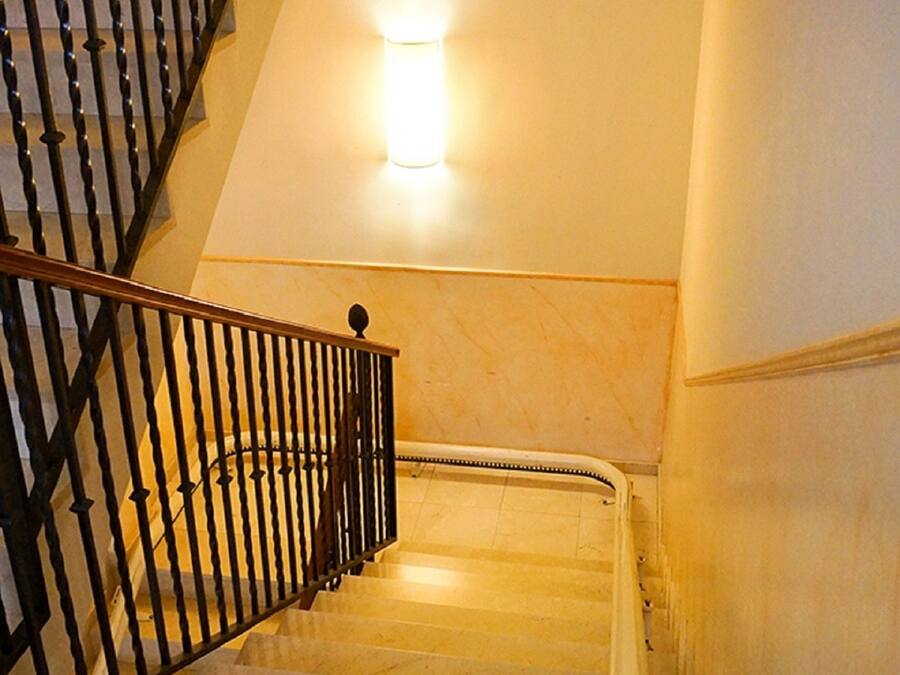 Uma escada com corrimão, luminária e placa fixada na parede.