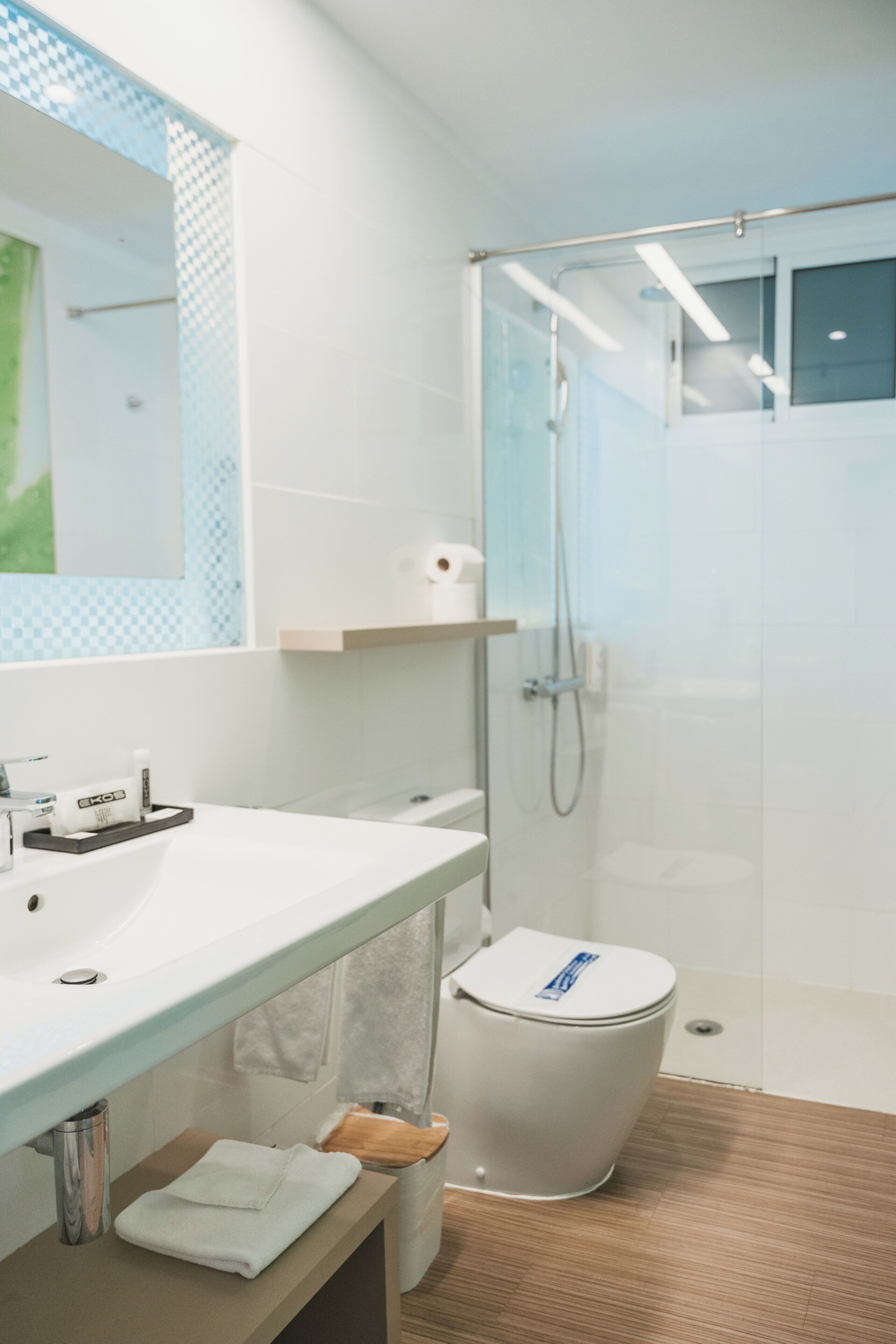 Casa de banho moderna com cabine de duche em vidro, lavatório branco com dispensador de sabão e sanita com etiqueta azul.