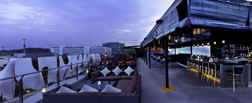 Um bar no terraço com mesas ao ar livre, área de bar e vista para o horizonte da cidade.