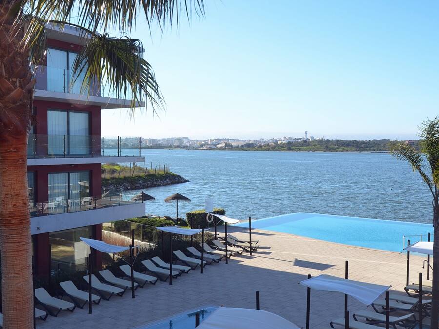 Um hotel moderno com piscina, espreguiçadeiras e vista para o mar.