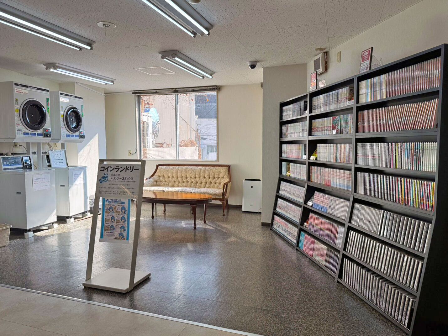 Uma biblioteca com sofá, estantes, máquina de lavar roupa e uma placa.