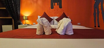 Quarto de hotel com cama, almofadas, mesa de cabeceira, abajur e uma parede com silhueta.