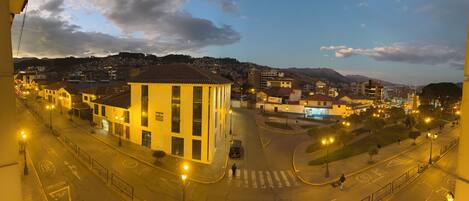 Vista urbana ao entardecer, com edifícios, ruas e uma faixa de pedestres.